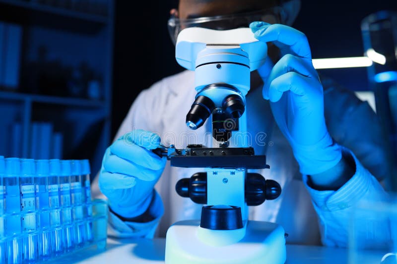 A Talented Scientist Sits in His Lab while Using a Microscope To Look ...