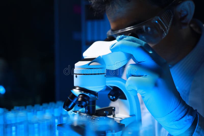 A Talented Scientist Sits in His Lab while Using a Microscope To Look ...