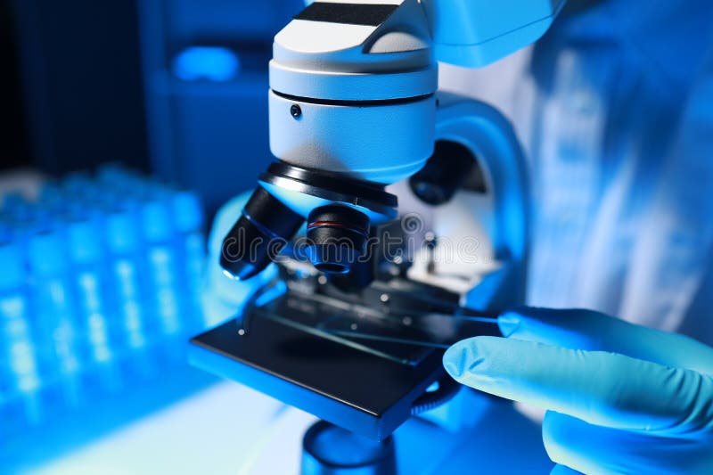 A Talented Scientist Sits in His Lab while Using a Microscope To Look ...