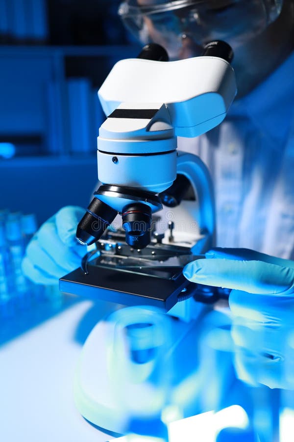 A Talented Scientist Sits in His Lab while Using a Microscope To Look ...