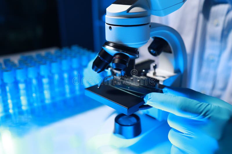 A Talented Scientist Sits in His Lab while Using a Microscope To Look ...