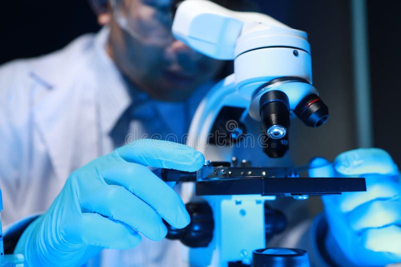 A Talented Scientist Sits in His Lab while Using a Microscope To Look ...