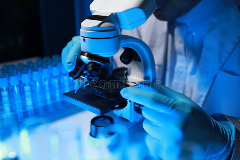 A Talented Scientist Sits in His Lab while Using a Microscope To Look ...