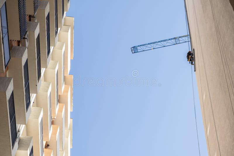 A Tall Building with Windows, Next To Which Workers Stand on a Crane ...
