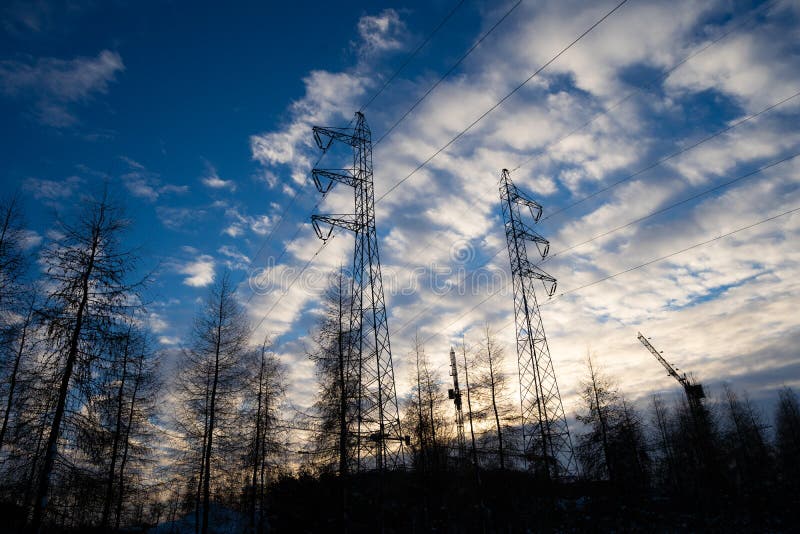 A Tall Construction Crane Against the Setting Sun. High Voltage Power ...