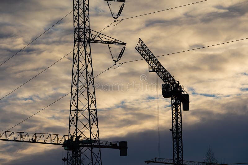 A Tall Construction Crane Against the Setting Sun. High Voltage Power ...