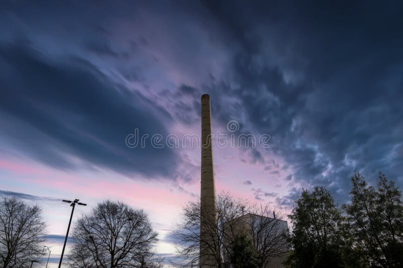 A Tall Thin Smoke Stack Surrounded by Bare Winter Trees and Lush Green ...