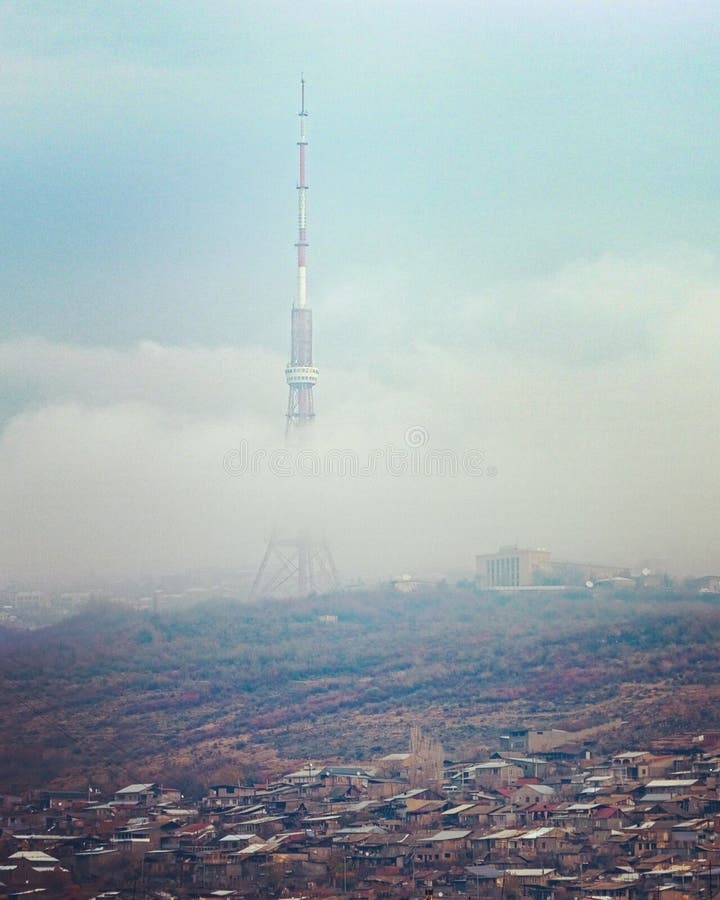 A Tall Tower Over the City Skyline in the Clouds with People Below it ...