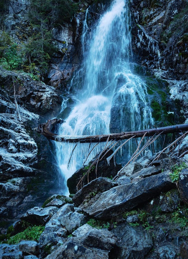 A Tall Waterfall Cascading Down Around Frozen Rocks Stock Photo - Image ...