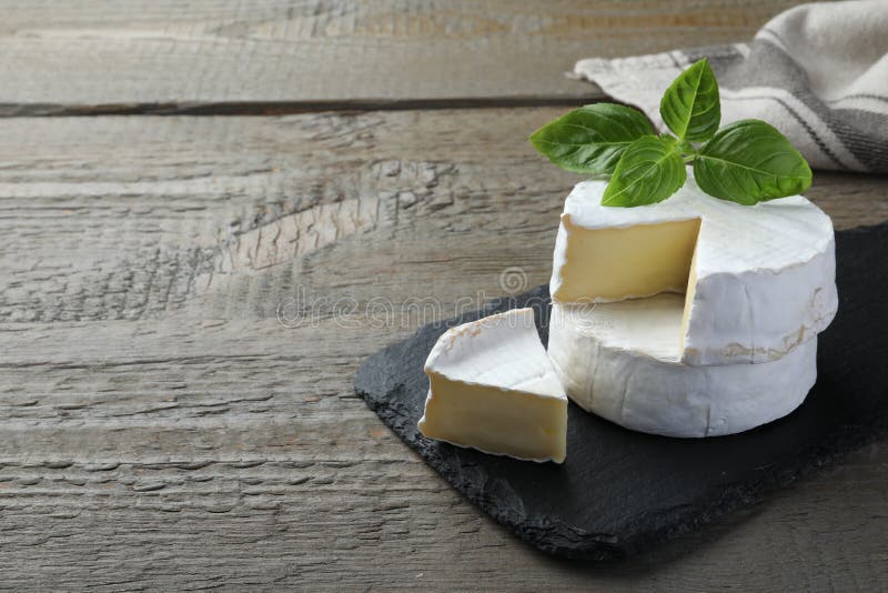 Tasty Cut and Whole Brie Cheeses with Basil on Wooden Table, Space for ...