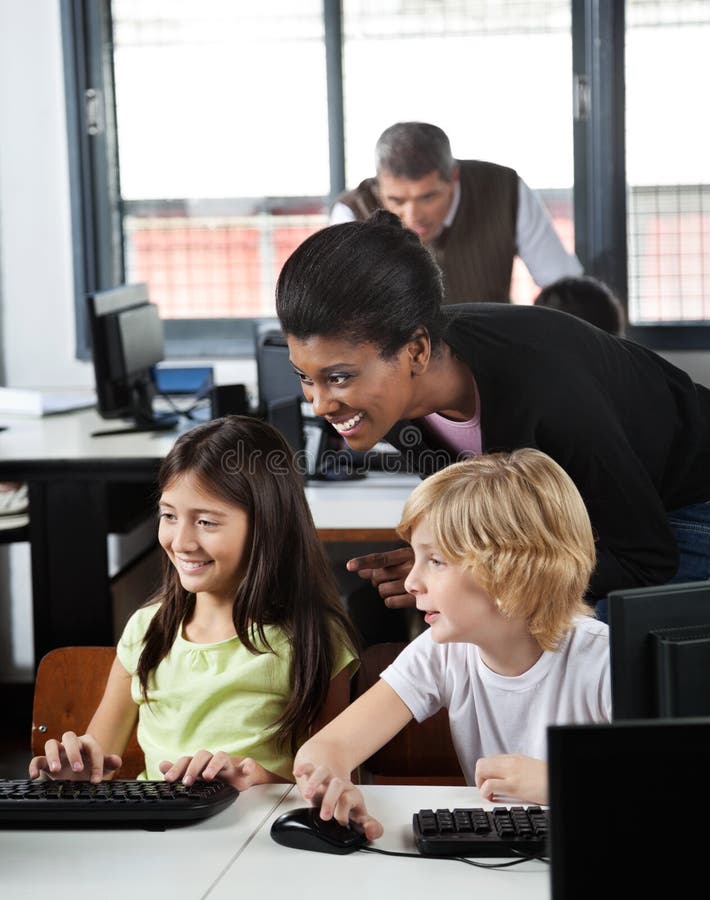 Teacher Assisting Schoolchildren in Using Desktop Stock Photo - Image ...