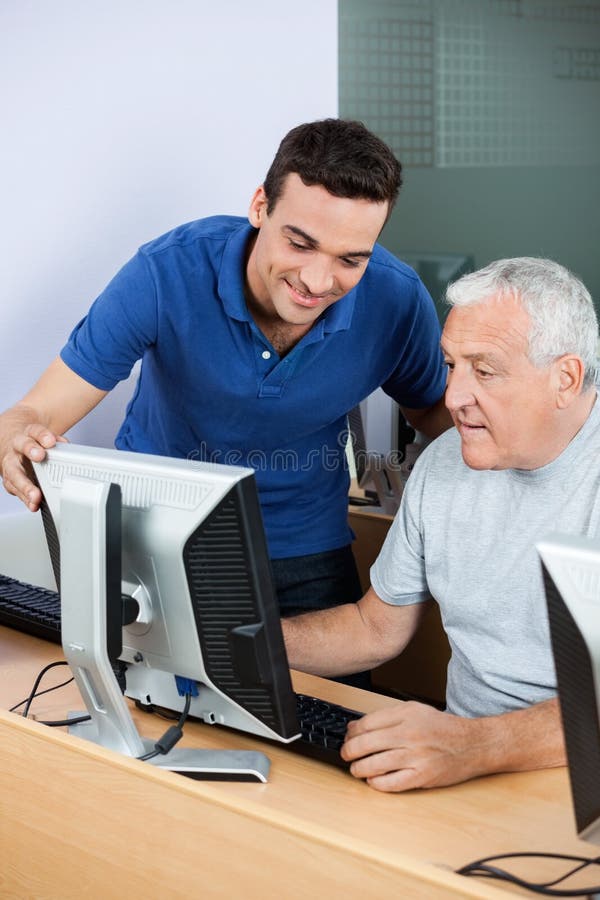 Teacher Assisting Senior Man in Using Computer at Classroom Stock Photo ...