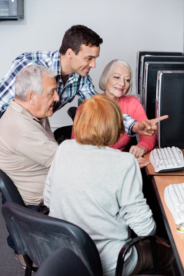 Teacher Assisting Senior Students in Using Computer at Classroom Stock ...