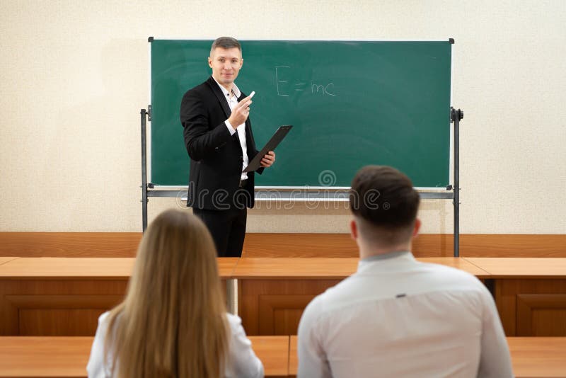 Teacher Giving a Lecture in a Classroom and Writing Math Formulas on ...