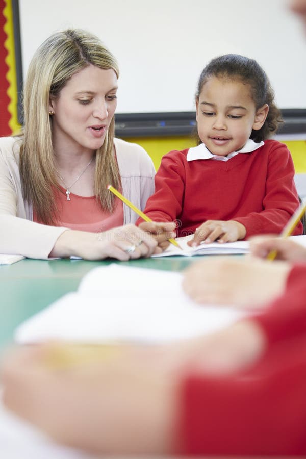 Teacher Helping Female Pupil with Writing Reading at Desk Stock Image ...