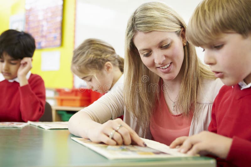 Teacher with Male Pupil Reading at Desk in Classroom Stock Image ...