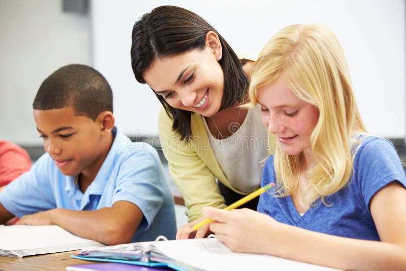 Teacher Helping Pupils Studying at Desks in Classroom Stock Photo ...