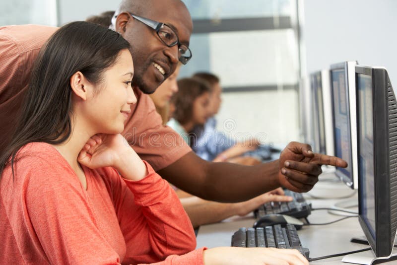 Teacher Helping Students Working at Computers in Classroom Stock Photo ...