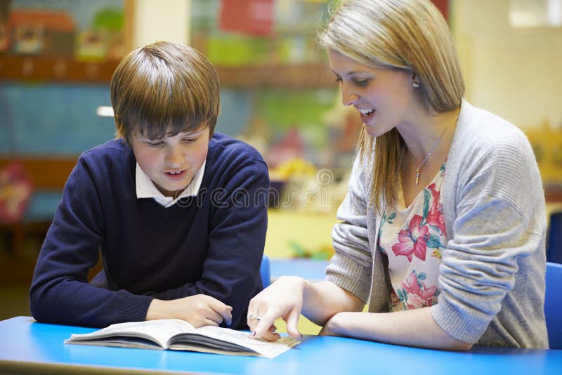 Teacher with Male Pupil Reading at Desk in Classroom Stock Image ... Teacher with Male Pupil Reading at Desk in Classroom Stock Image ...
