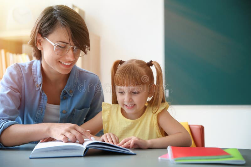 Teacher with Pupil Reading Book at Table in Classroom Stock Photo ...