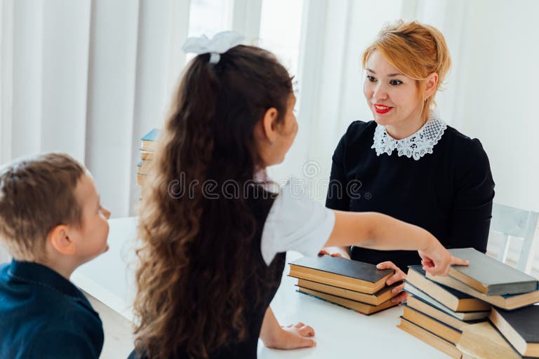 The Teacher and Schoolchildren with Books at the Table are Studying ...