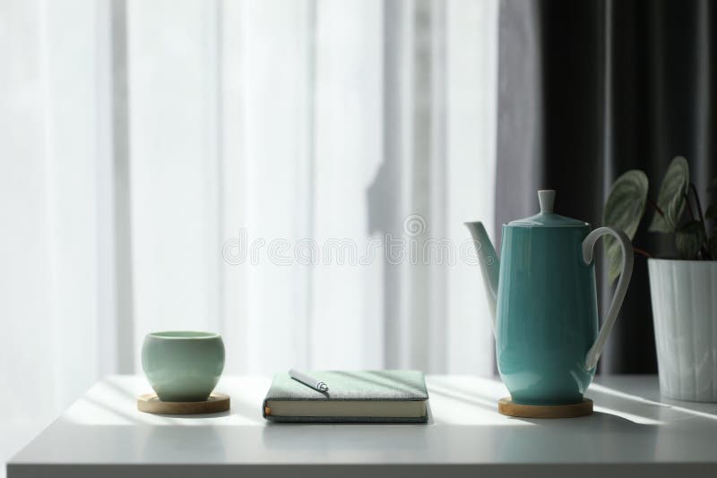 Teal Cup and Tall Teapot with Notebook and Silver Pen on White Table ...