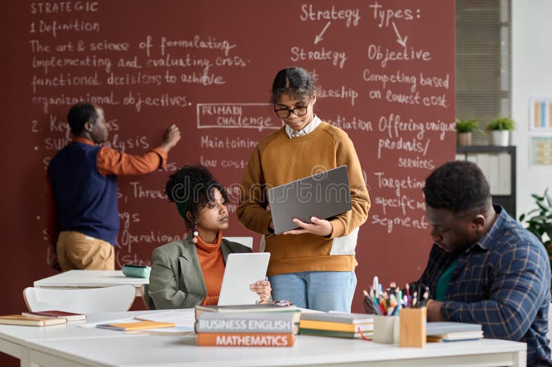 Two Black Girls Talking To Professor Standing by Blackboard in Class ...