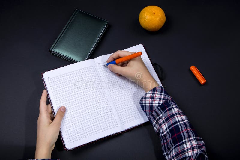 Open Notebook in the Hands of a Teenager Next To a Pen and Tangerine ...