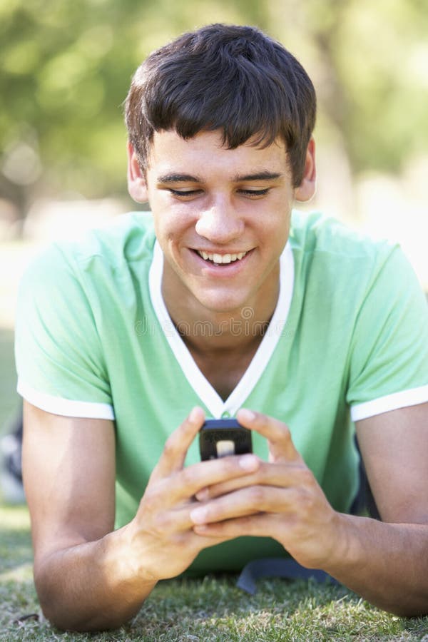 Teenage Boy Laying in Park Reading Text Message on Mobile Phone Stock ...