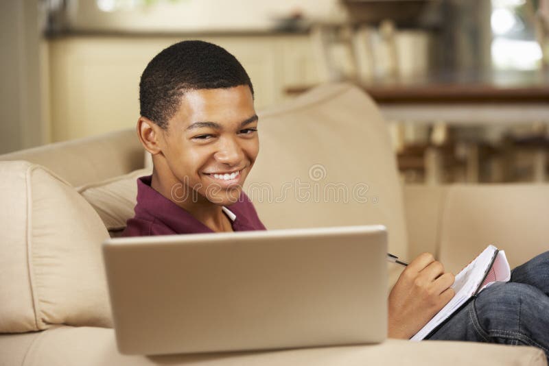 Teenage Boy Sitting on Sofa at Home Doing Homework Using Laptop ...