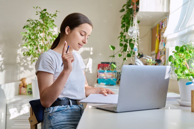 Teenage Girl Studying at Home Using Laptop Making Notes in Notebook ...