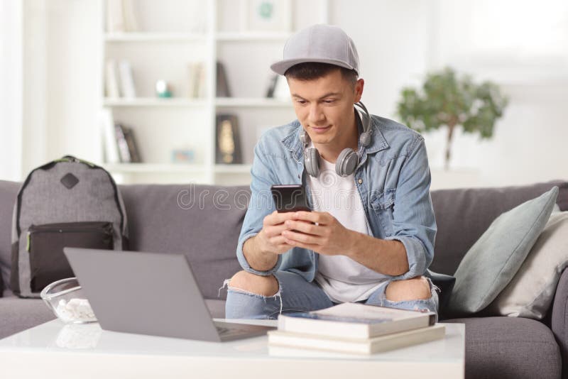 Teenager Using a Smartphone and Sitting on a Sofa with a Laptop ...