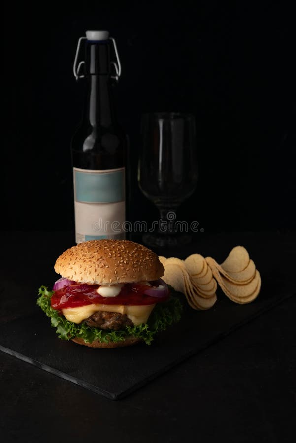 There is a Burger on a Dark Background, a Blurred Image of Chips and a ...