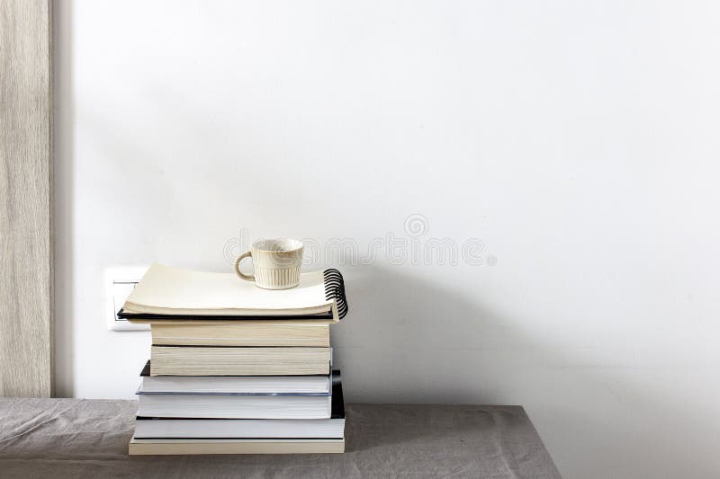 There is a Stack of Books on Beige Table Against a White Wall ...