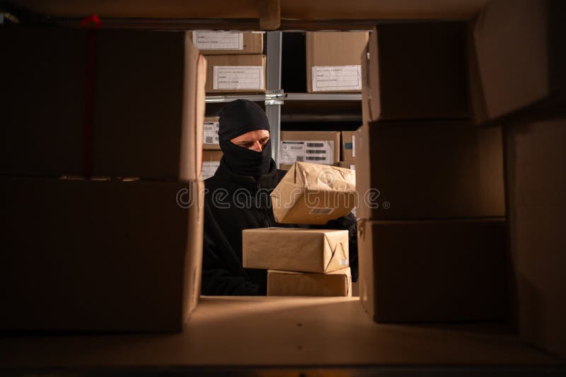 A Night Thief in a Black Mask Steals Boxes of Goods in a Warehouse ...