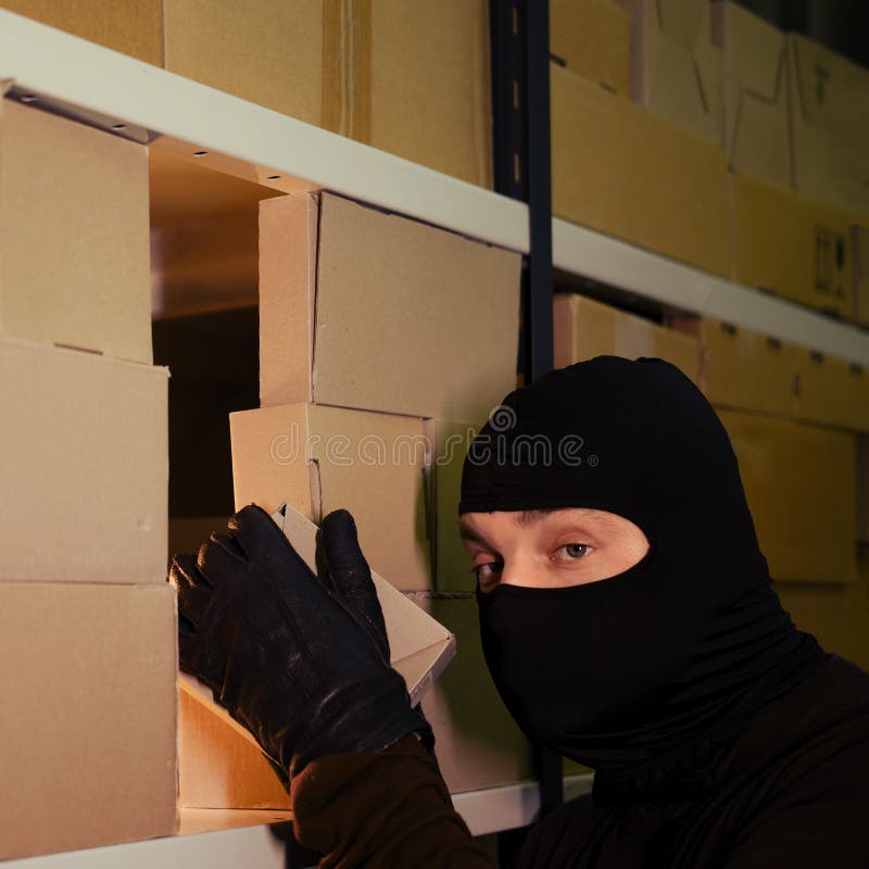 Thief in a Black Ski Mask Steals a Box with a Parcel in a Warehouse at ...
