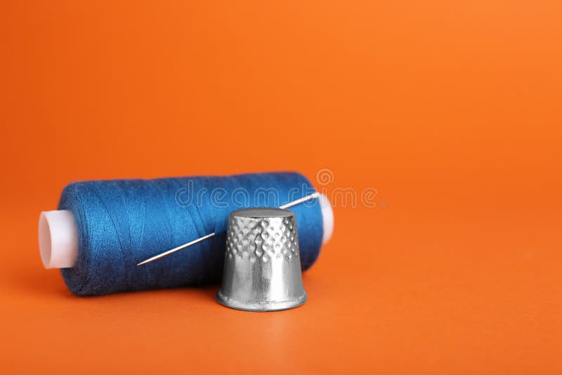 Thimble and Spool of Blue Sewing Thread with Needle on Orange ...