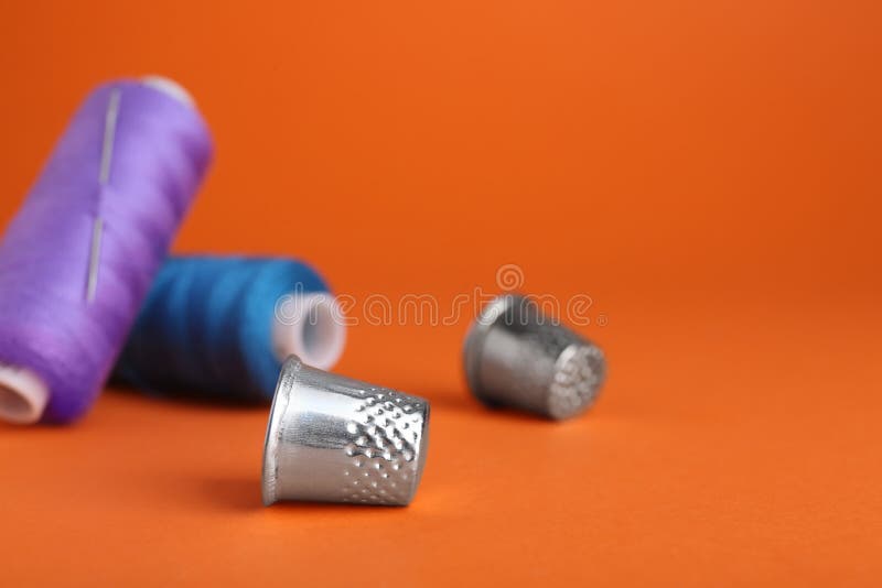 Thimbles, Spools of Sewing Threads and Needle on Orange Background ...