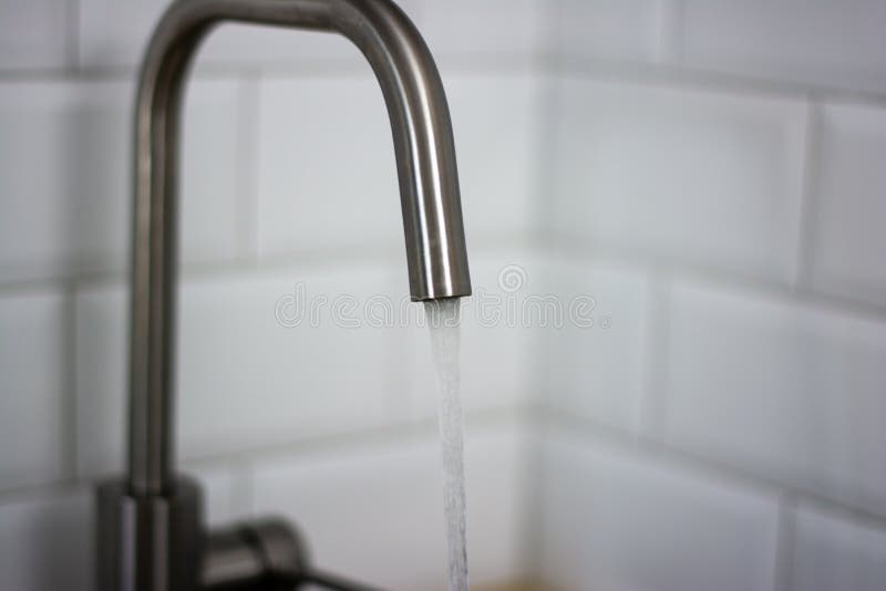 Thin Stream of Water Flowing from the Tap Against a White Tile in the ...