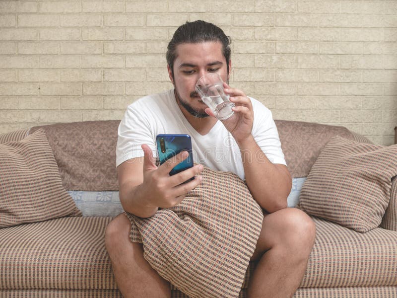 A Thirsty Man Browses His Phone while Drinking a Glass of Water and ...