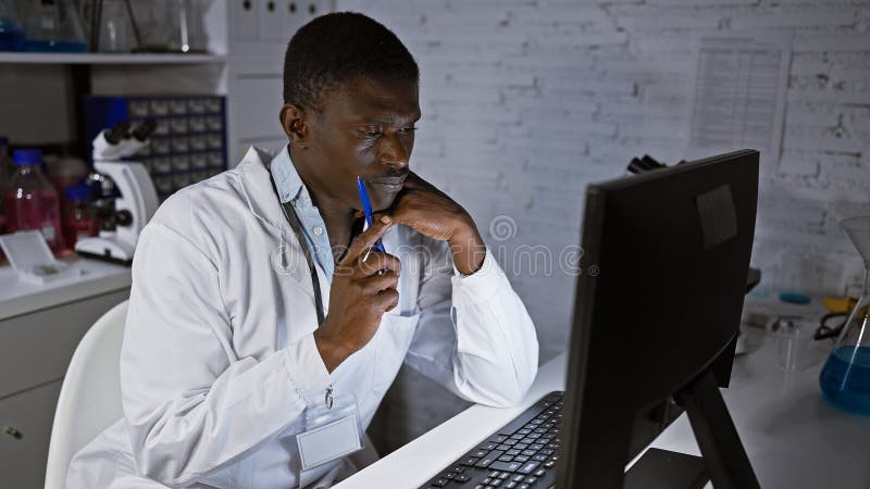 A Thoughtful African Man in a Lab Coat Analyzes Data on a Computer in a ...