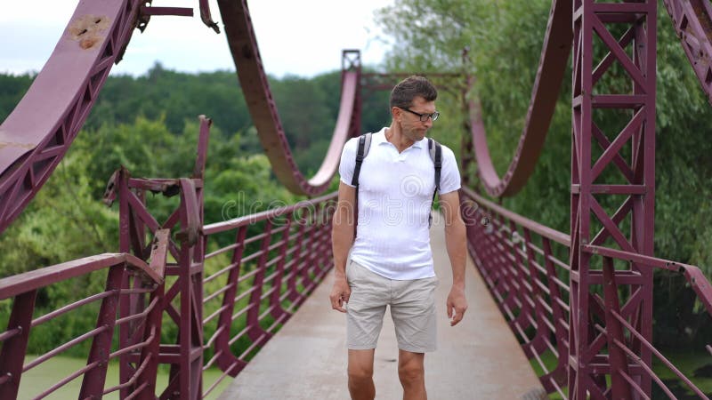 Thoughtful Caucasian Man Walking on Bridge in Park Looking Around and ... Thoughtful Caucasian Man Walking on Bridge in Park Looking Around and ...