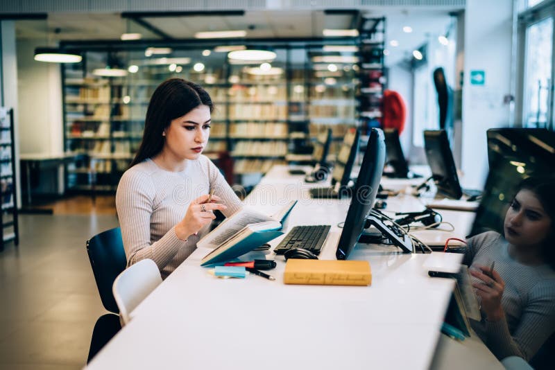 Thoughtful Female Student Reading Textbook and Using Computer while ...