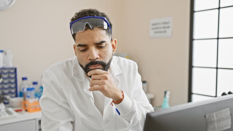 Thoughtful Hispanic Man with a Beard in Lab Goggles Contemplates in a ...