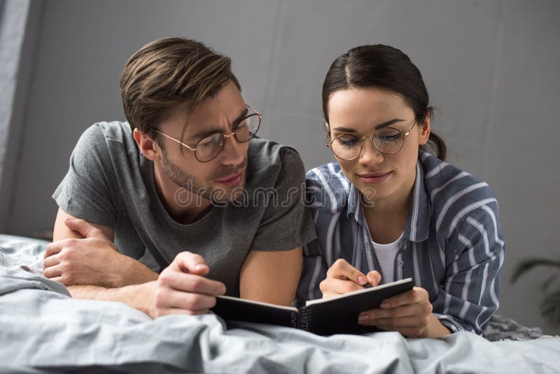 Thoughtful Man Looking At Woman Writing In Notepad While Lying Stock