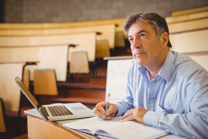Thoughtful Professor Writing in Book at Desk Stock Image - Image of ...