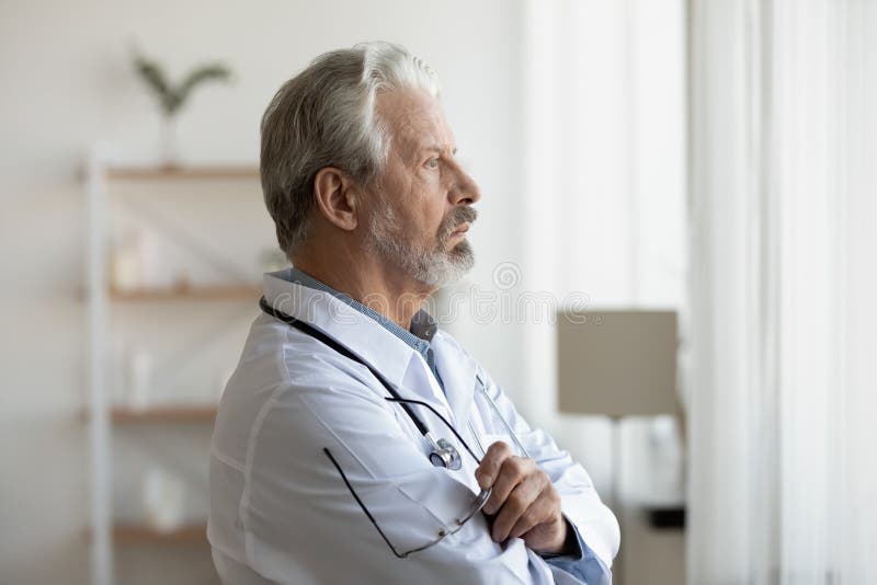 Thoughtful Serious Senior Doctor Looking through Window Lost in ... Thoughtful Serious Senior Doctor Looking through Window Lost in ...