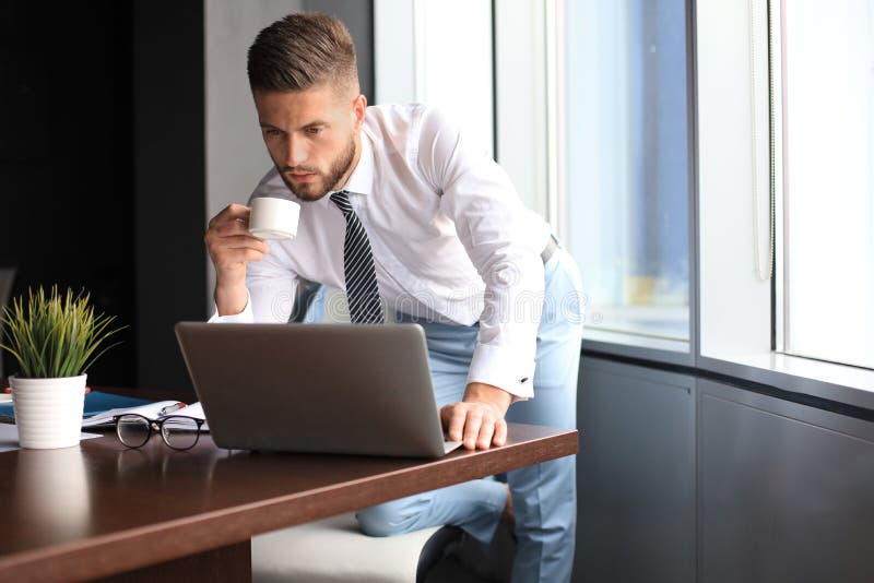 Thoughtful Young Business Man is Using Computer and is Drinking Coffee ...