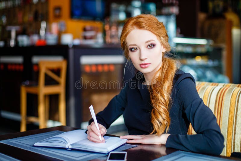 Thoughtful Young Businesswoman Sitting in a Cafe and Writing in Notepad ...