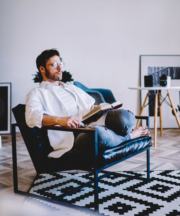 Thoughtful Young Man with Paper Book in Hand Taking Rest in Apartment ...